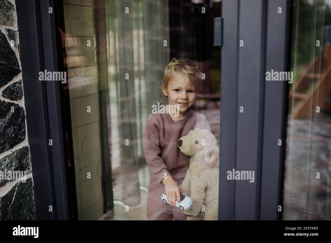 Happy little child standing with teddy bear behind the window, photo ...