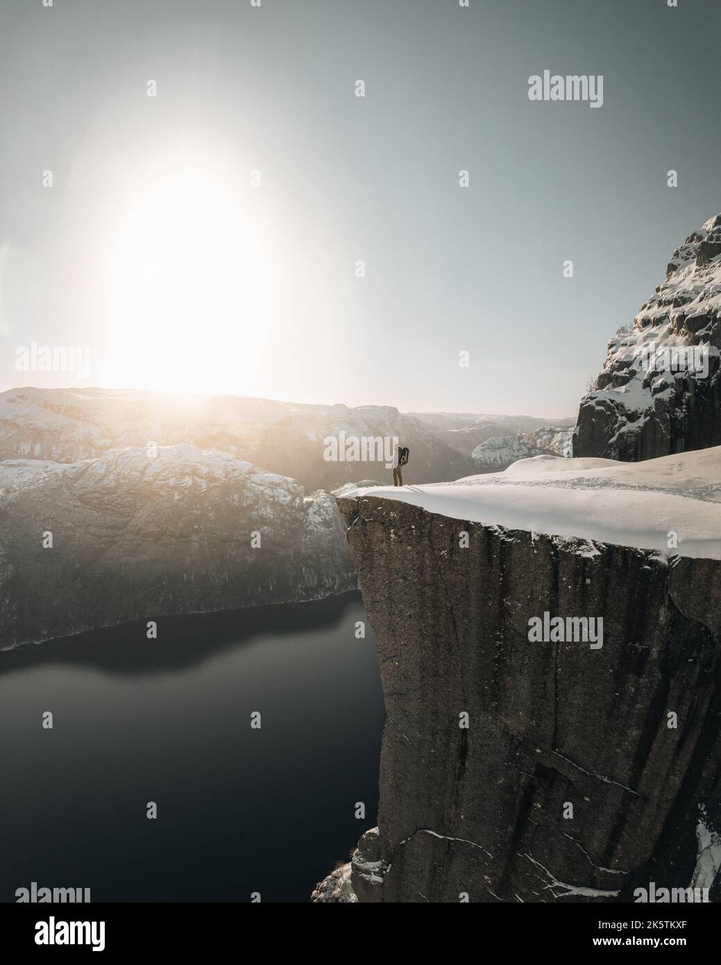An aerial view of human standing on the snow covered edge of cliff ...