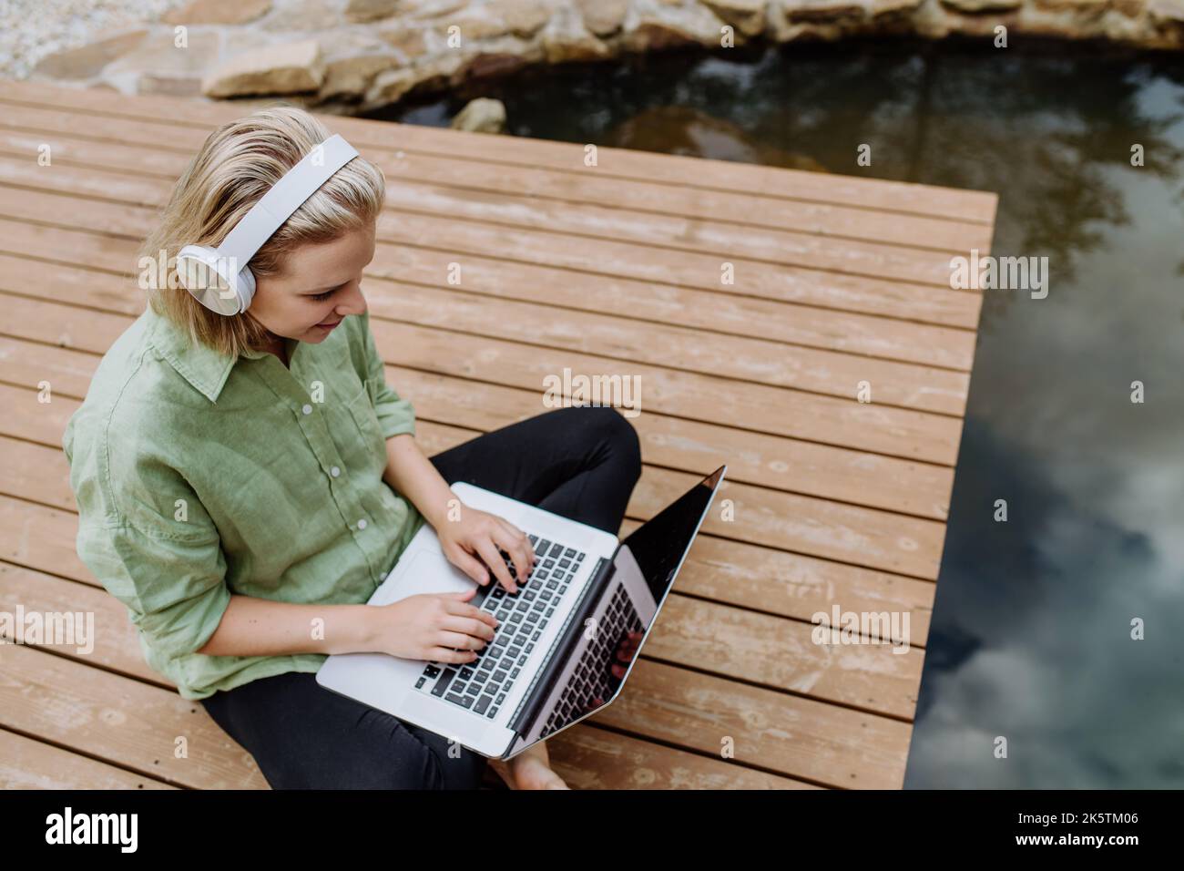 Woman, freelancer working on laptop, sitting on a pier by the backyard ...