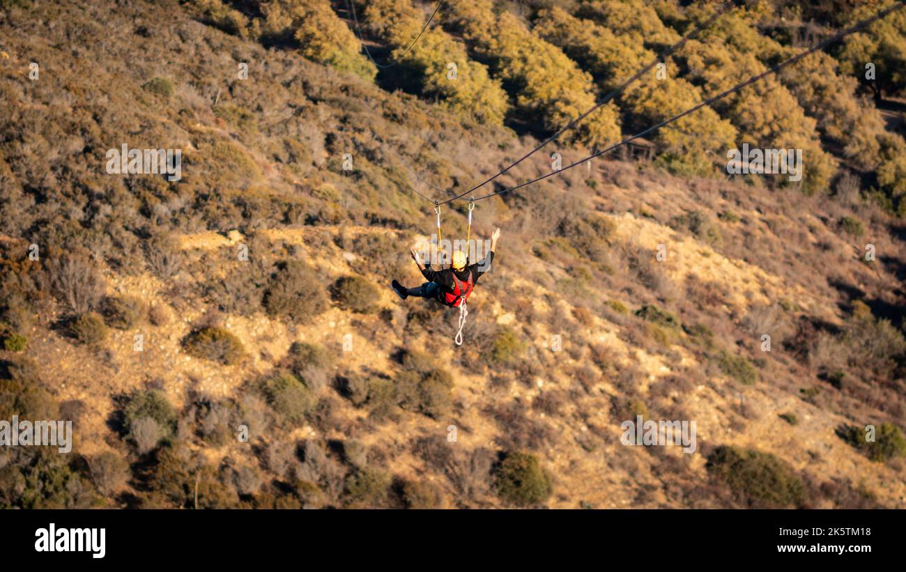 A back view of human flying with zipline over greenery mountains Stock ...