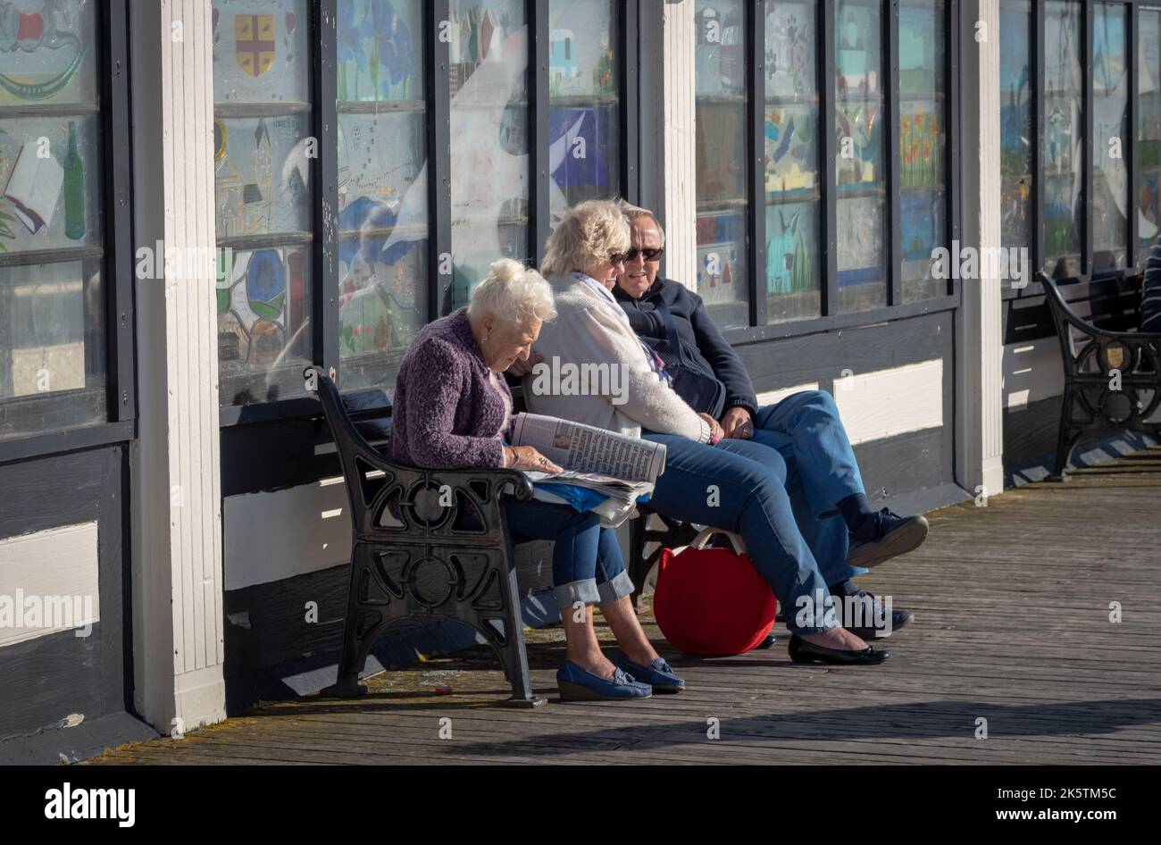 An elderly woman sits on a public bench to read a newspaper next to a ...