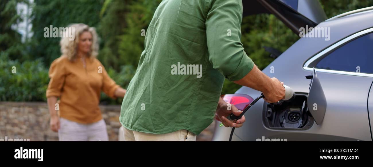 Man holding power supply cable, while his wife waiting for car charging ...