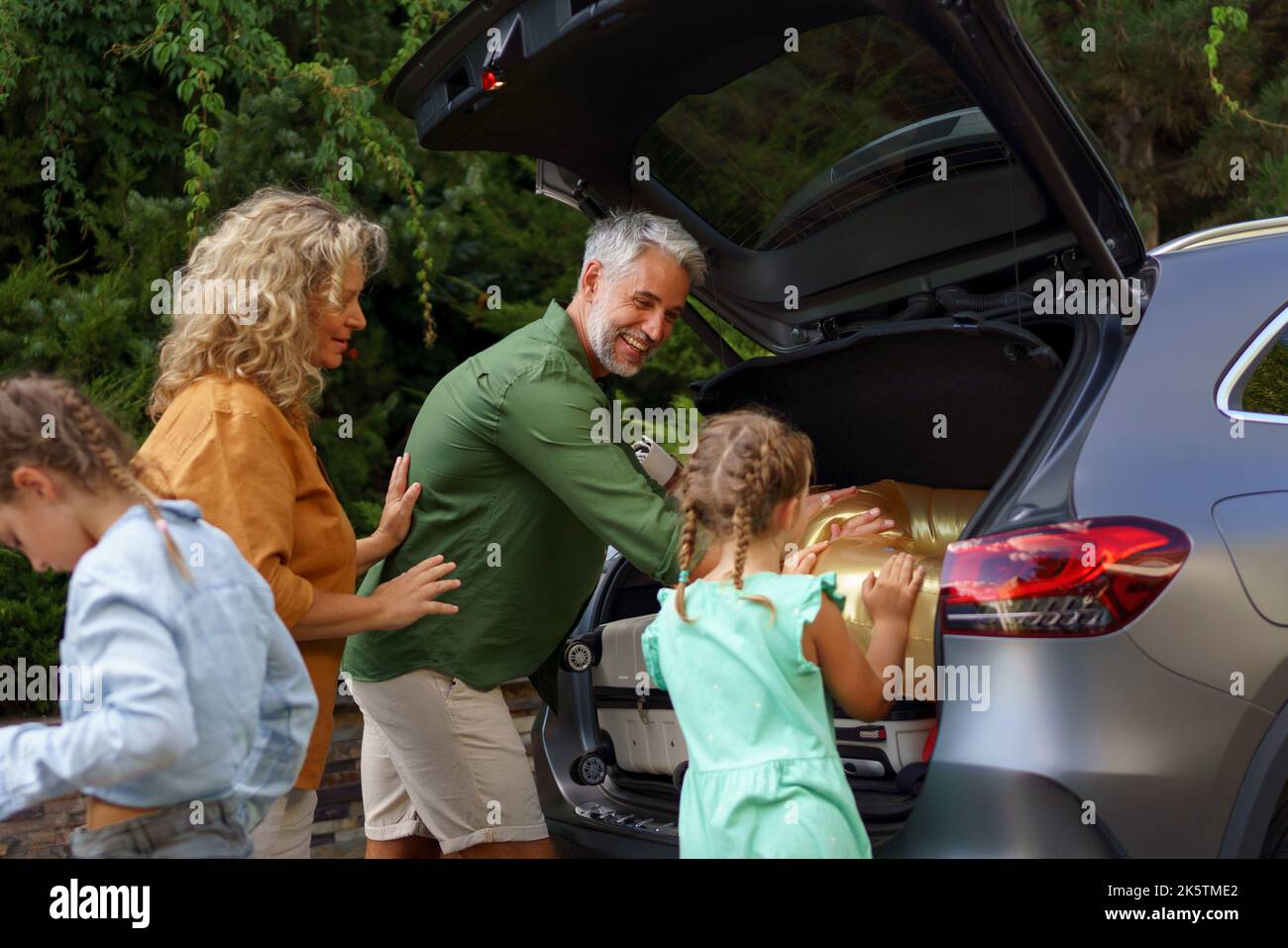 Happy family preparing for holiday, putting suitcases in car trunk ...