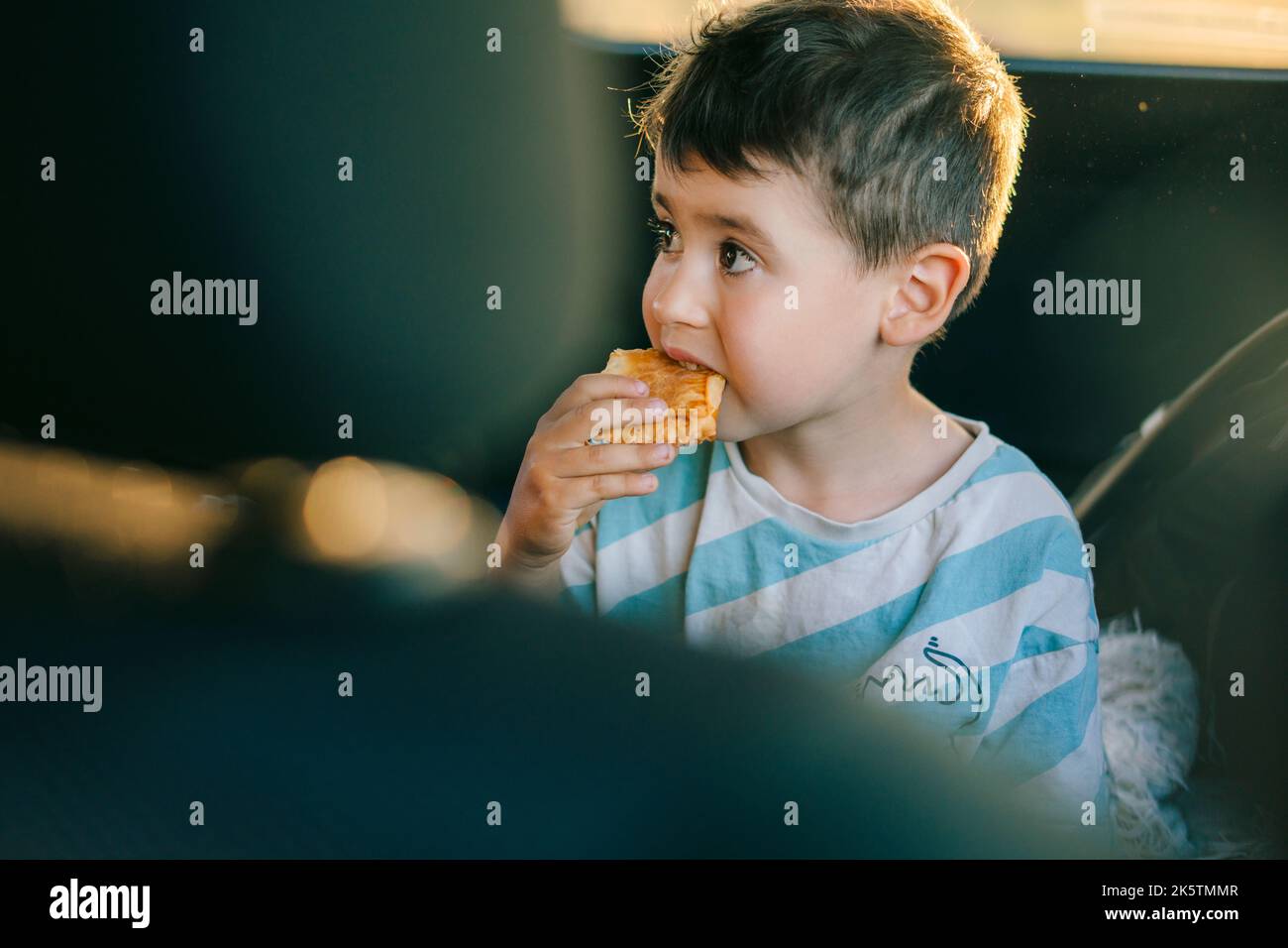 Portrait of a boy sitting in back seat of family car eating pie and ...