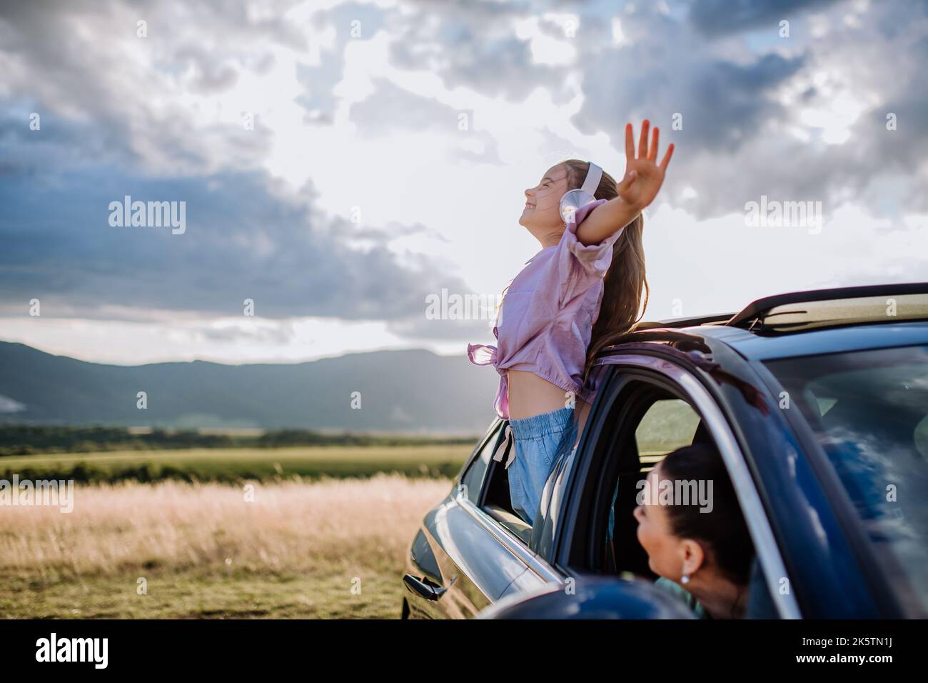 Little girl with headphones standing and leaning out of the car window ...