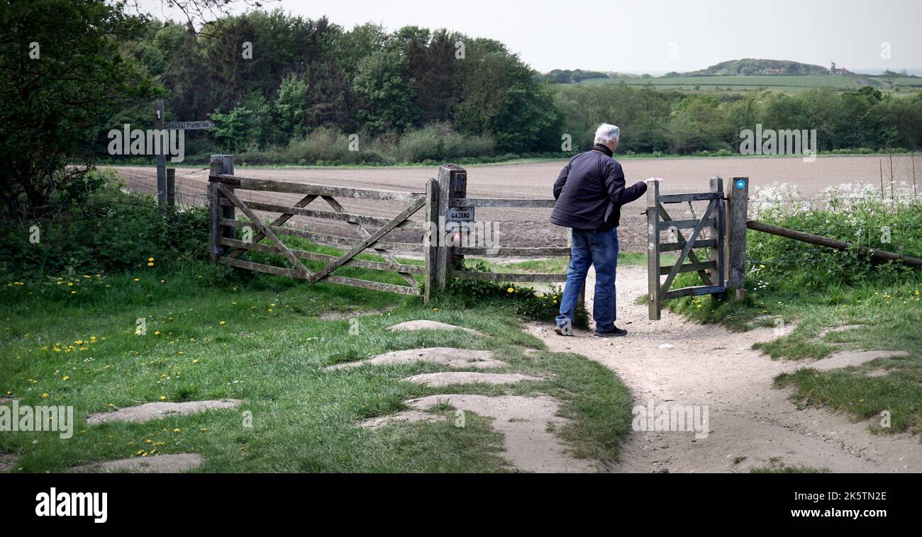 lone older man walking through gate at sheeringham on coastal footpath ...