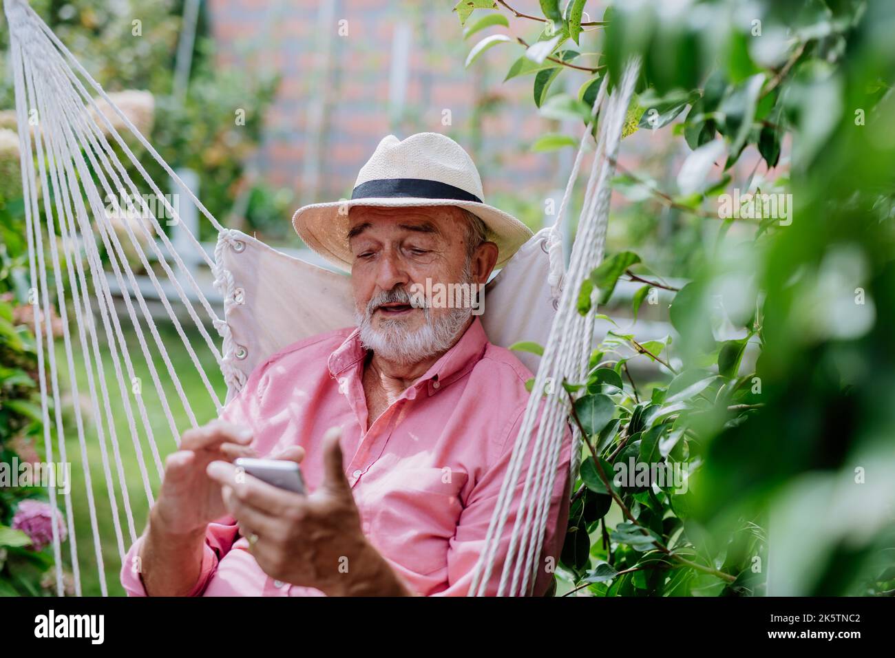 Happy senior man sitting in outdoor garden swing and scrolling ...
