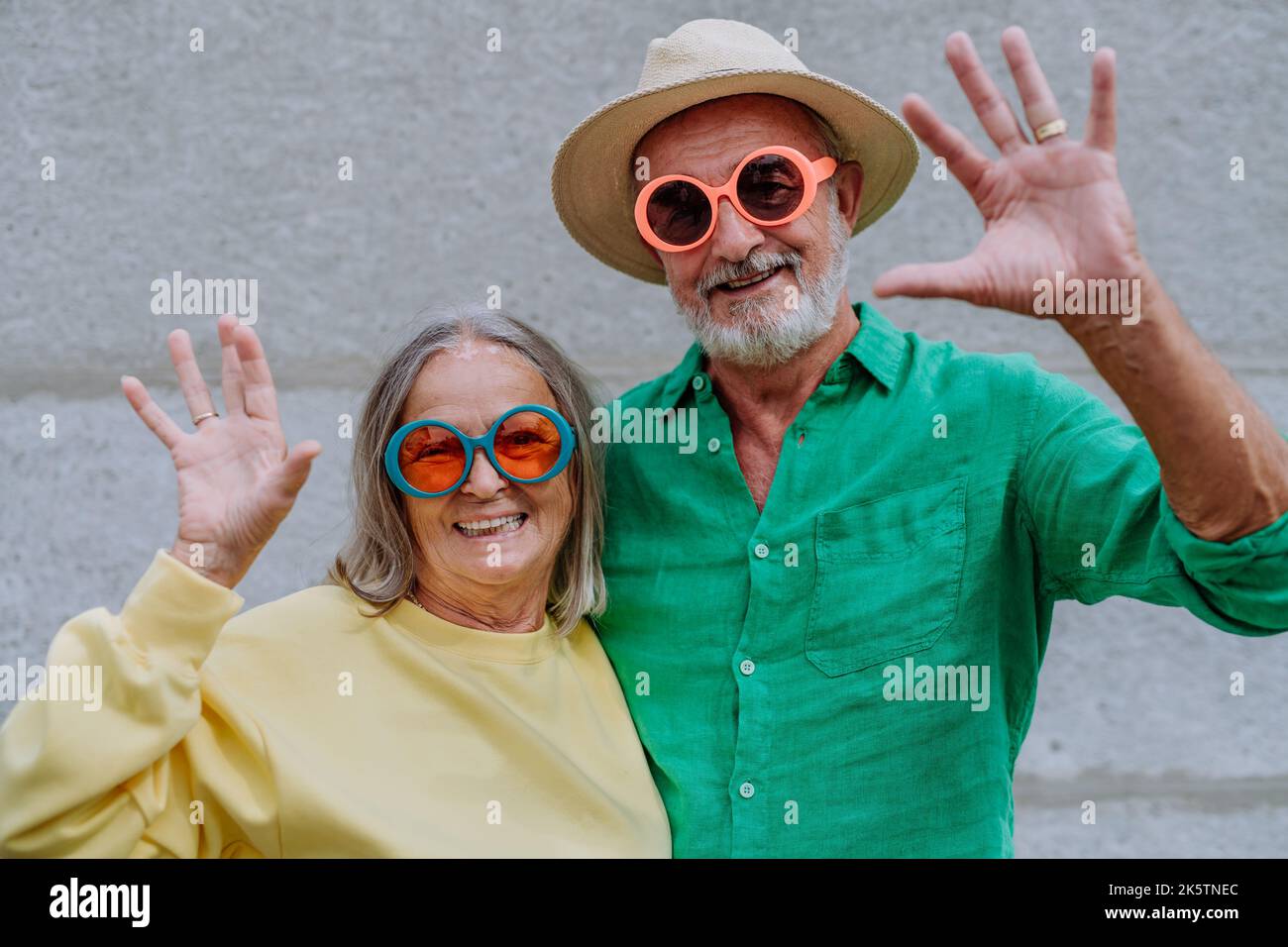 Portrait of happy seniors couple in colourful clothes waving at camera ...