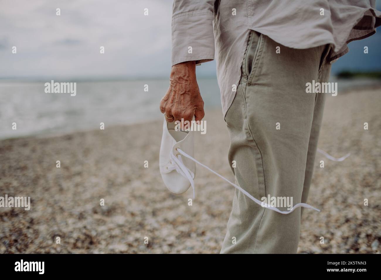Low section of senior woman standing at beach with taking off shoes ...