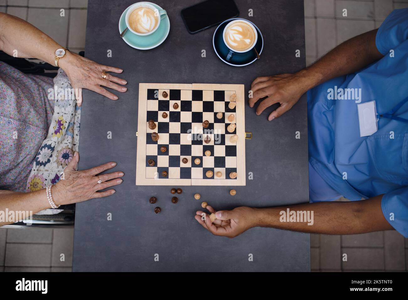 Top view of caregiver playing chess and drinking coffe with his client ...