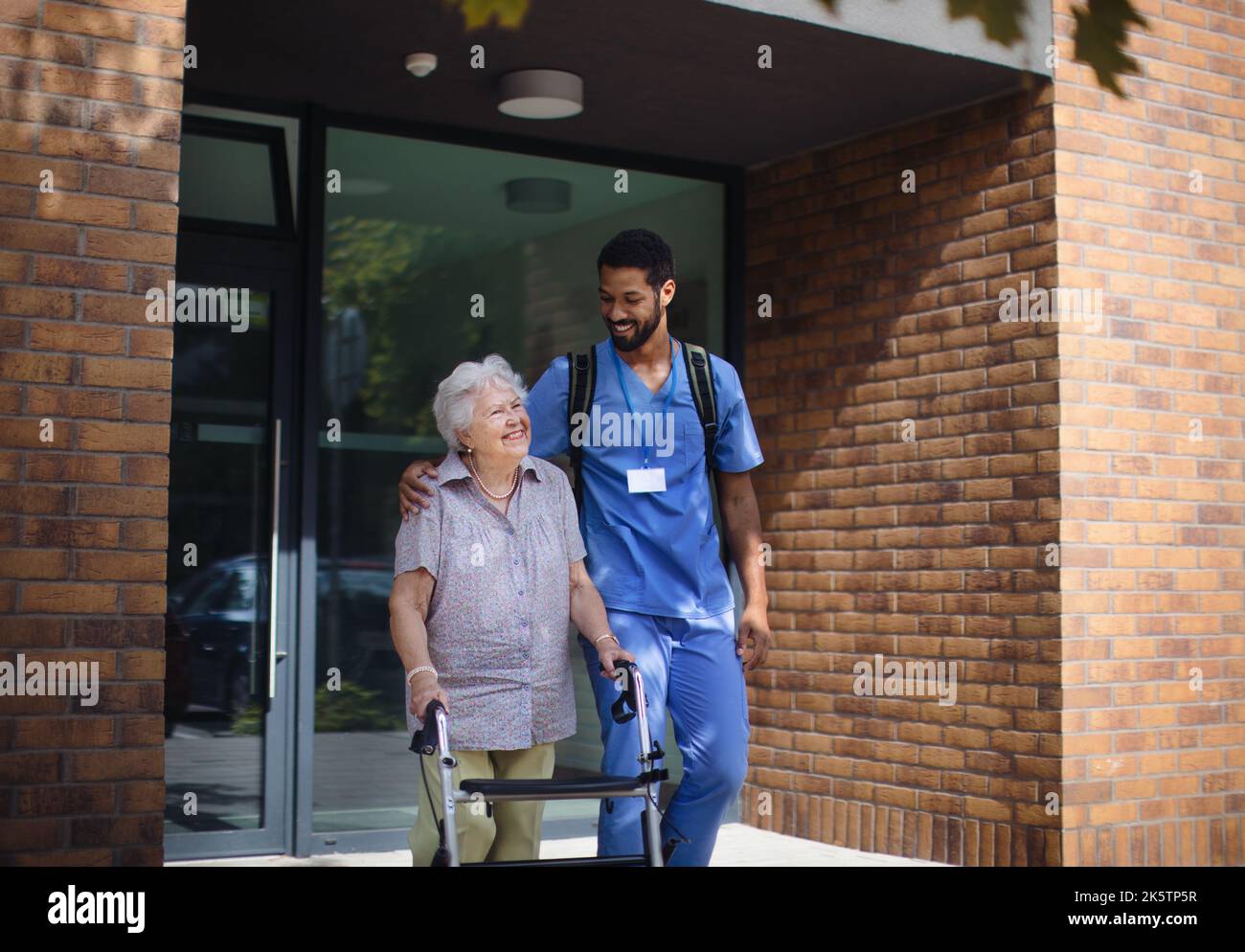 Caregiver walking with senior woman client in front of nurishing home ...