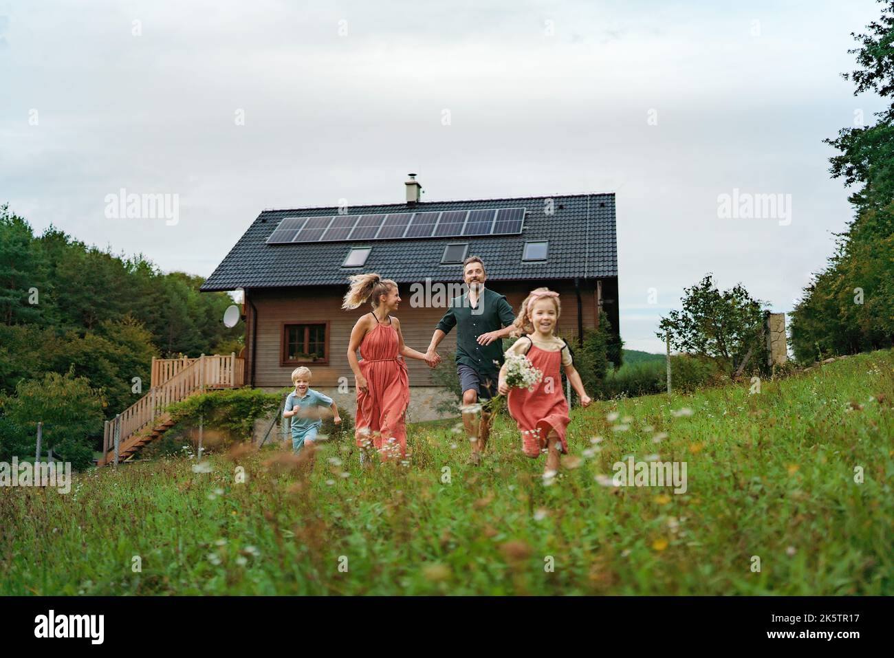 Happy family running near their house with solar panels. Alternative ...
