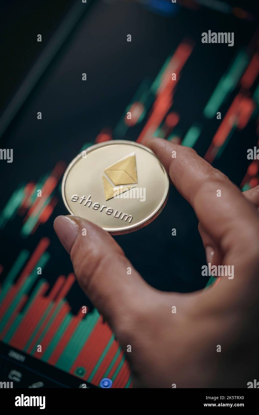 Hand holding a silver Ethereum (ETH) cryptocurrency coin with candle ...