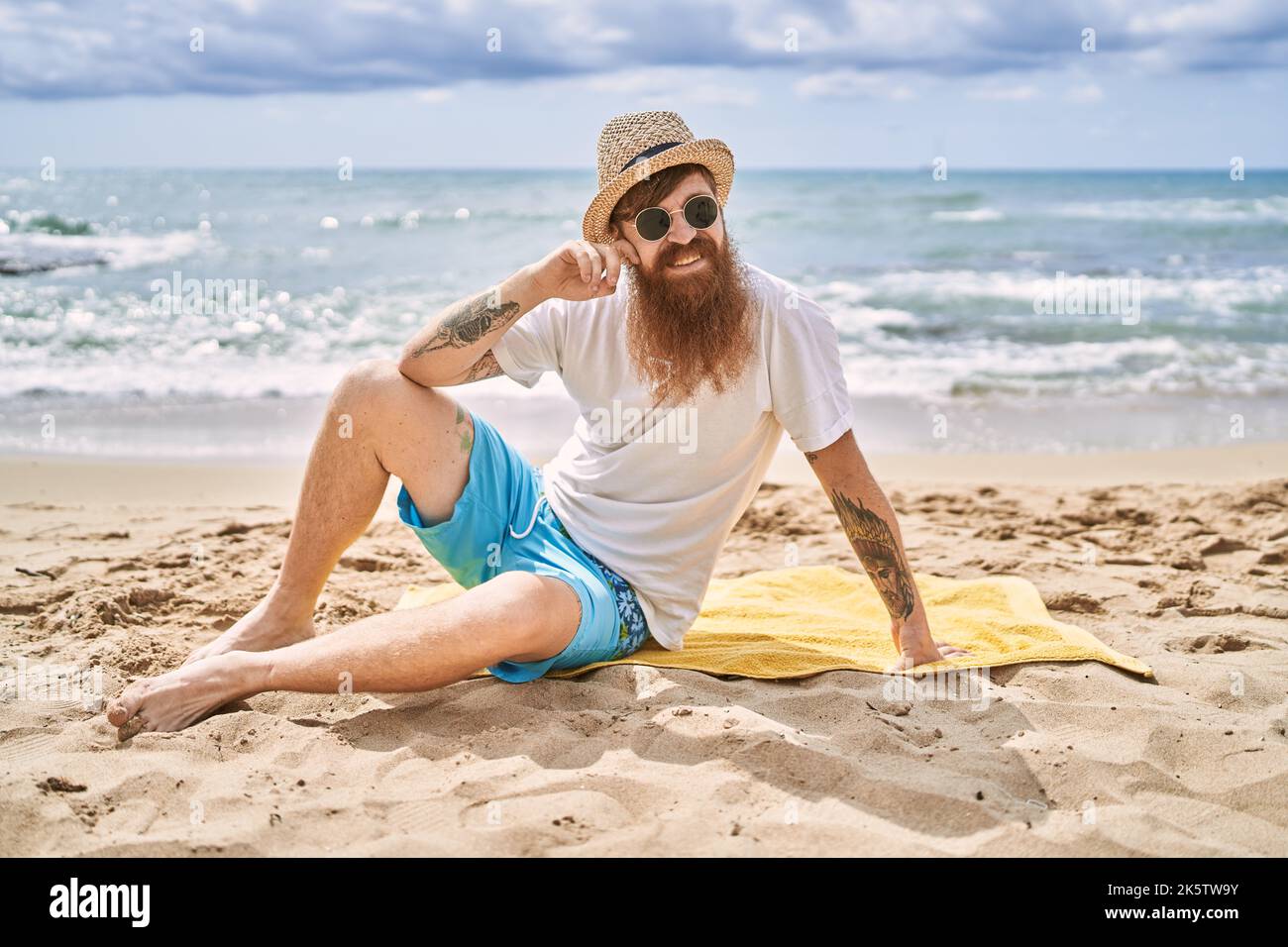 Young redhead man smiling happy sitting on the towel at the beach Stock ...