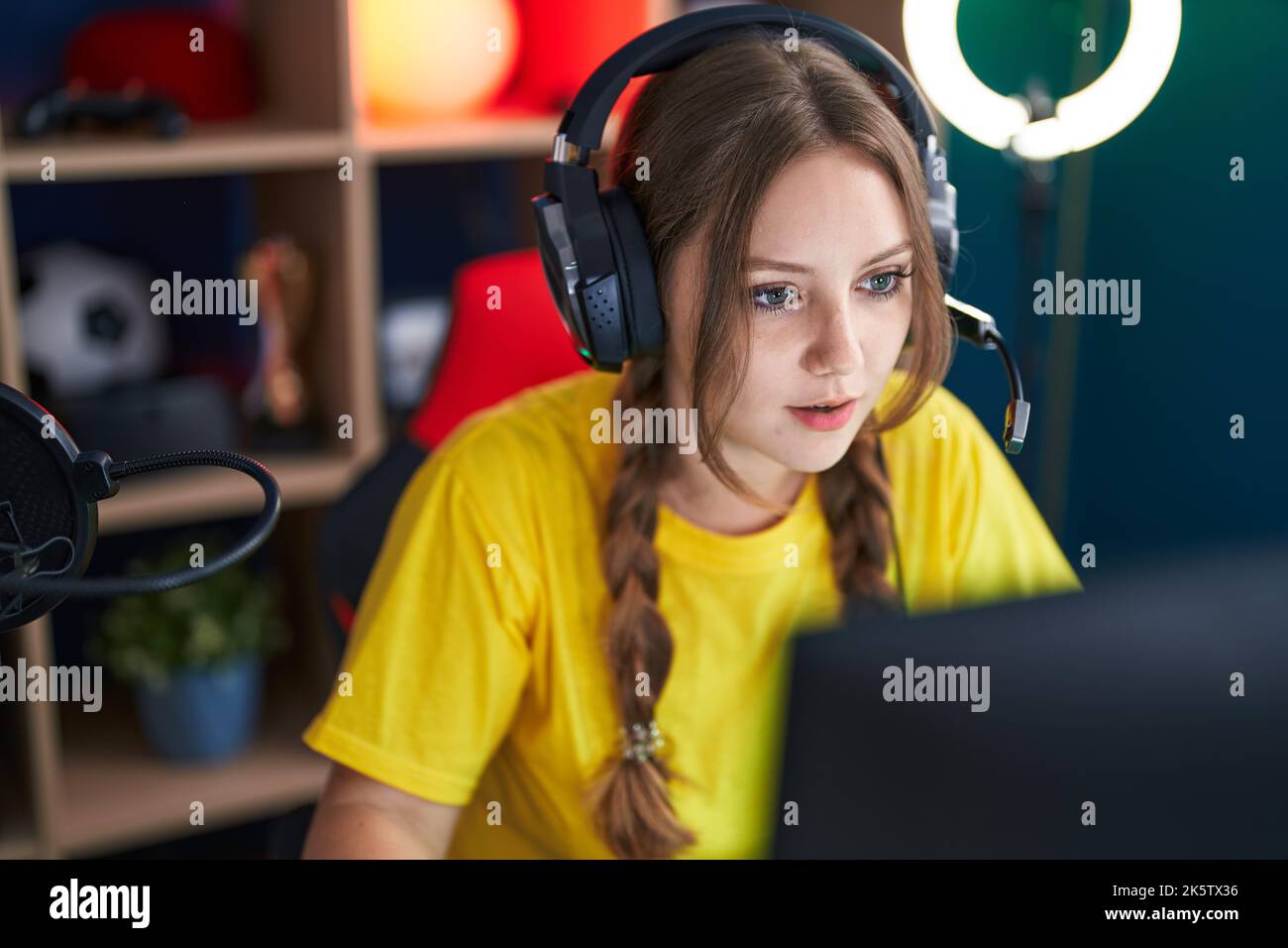 Young blonde woman streamer playing video game using computer at gaming ...