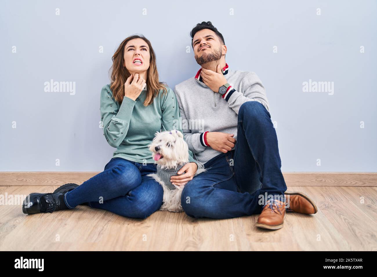 Young hispanic couple sitting on the floor with dog touching painful ...