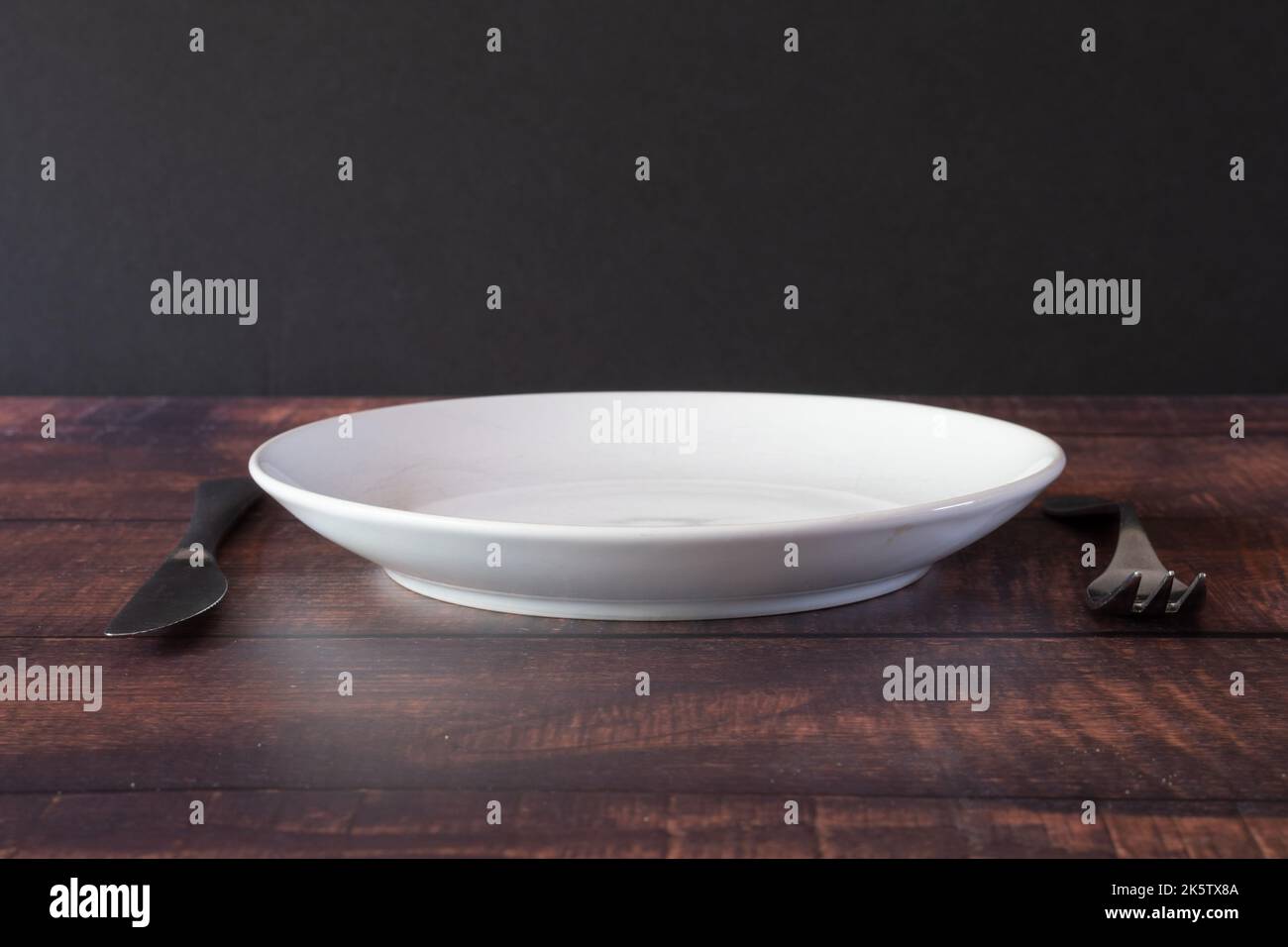 A white porcelain plate and silver flatware set on a rustic brown table ...