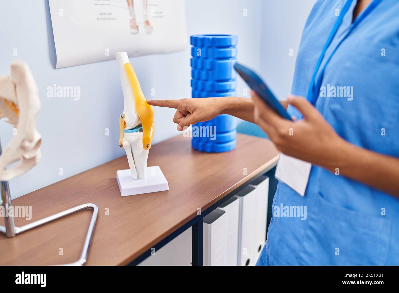 Young hispanic woman physiotherapist using smartphone pointing to ...