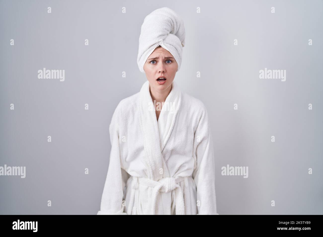 Blonde caucasian woman wearing bathrobe afraid and shocked with ...