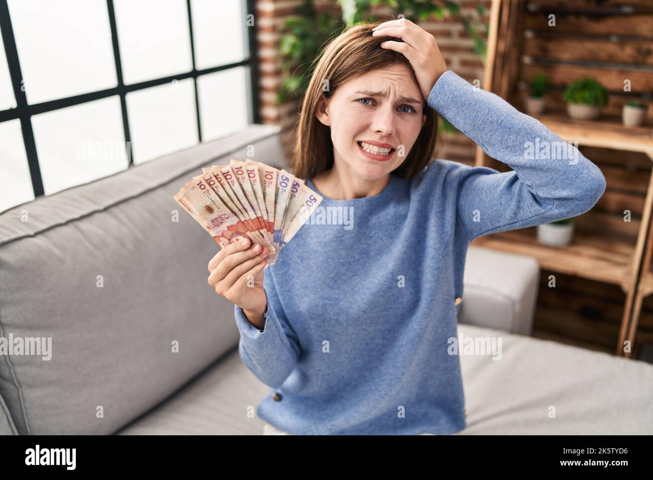 Young brunette woman holding colombian pesos stressed and frustrated ...