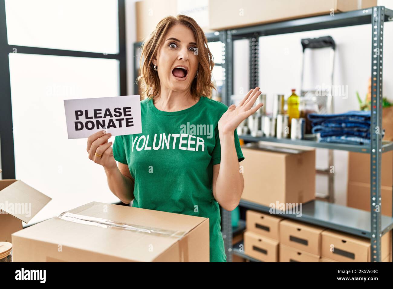 Middle age woman wearing volunteer t shirt holding please donate banner ...