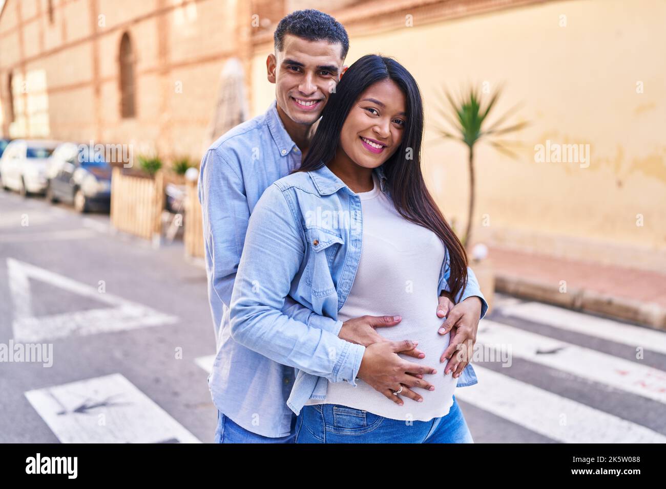 Young latin couple expecting baby hugging each other standing at street Stock Photo - Alamy