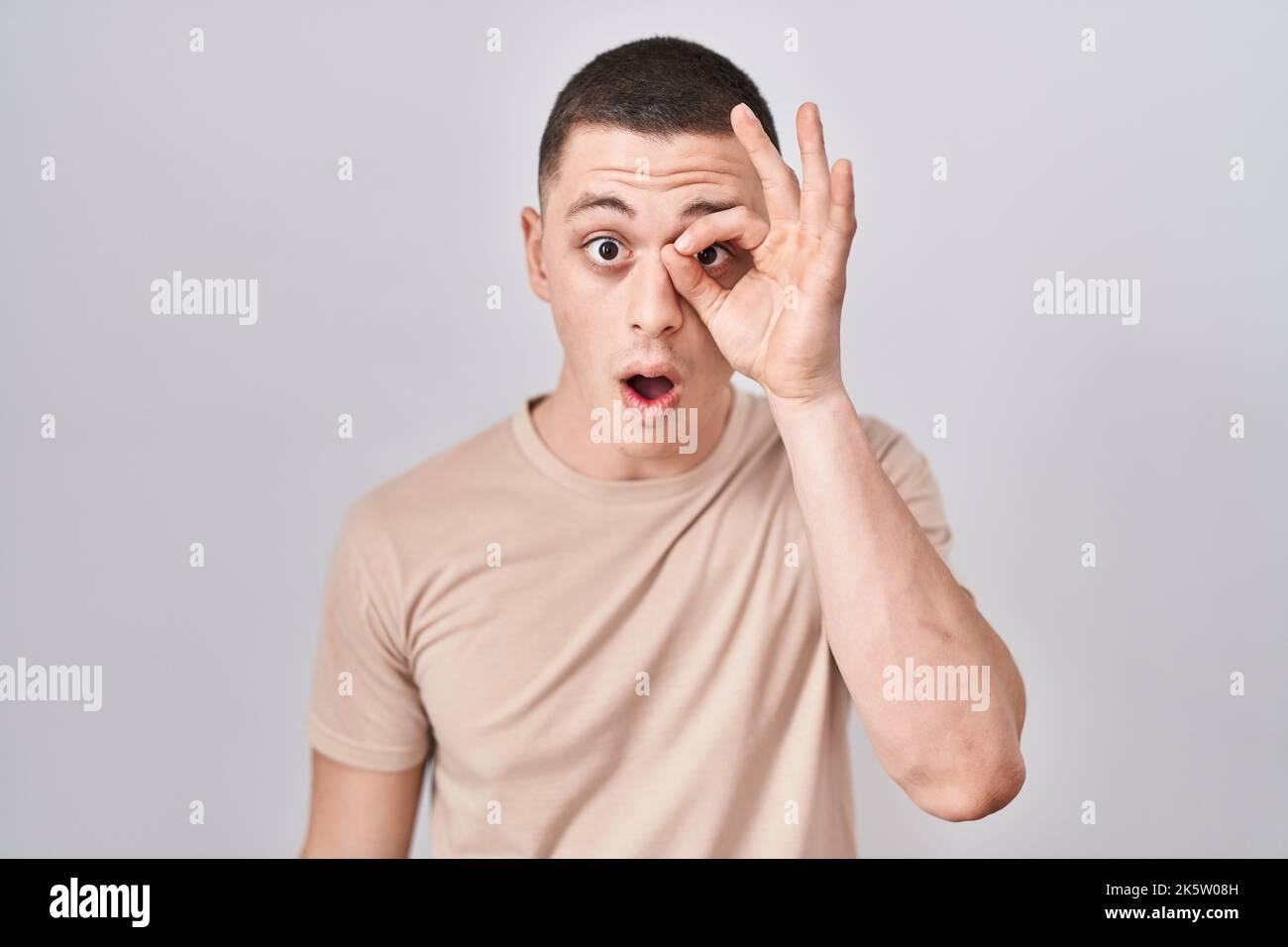 Young man standing over isolated background doing ok gesture shocked ...