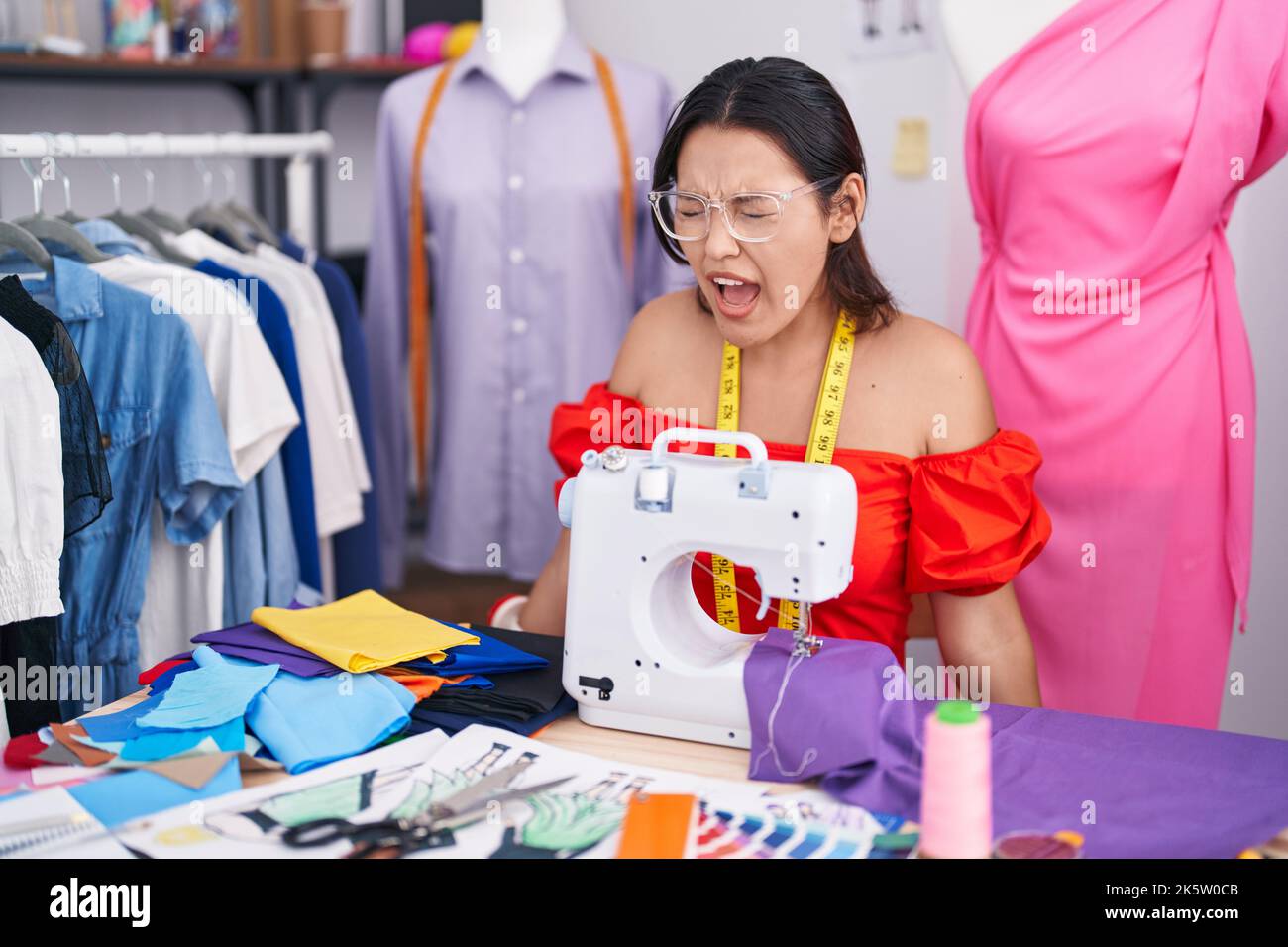 Hispanic young woman dressmaker designer using sewing machine angry and ...