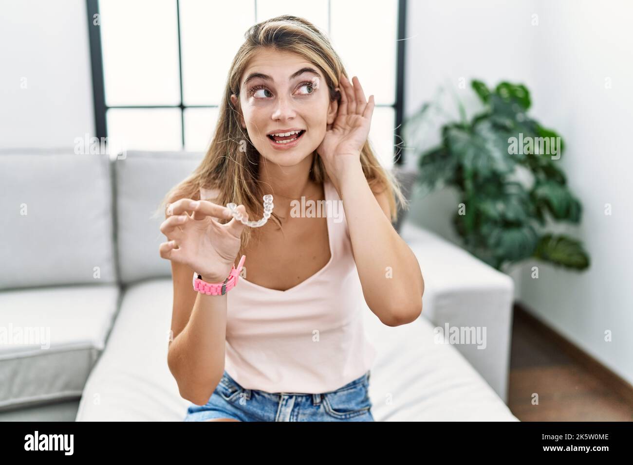Young blonde woman holding invisible aligner orthodontic smiling with ...