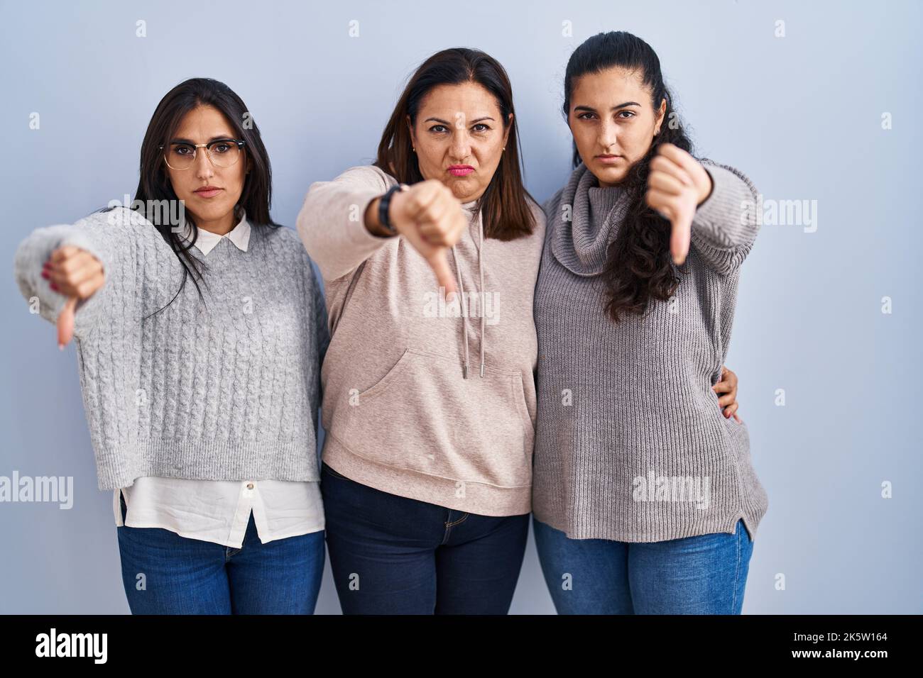 Mother and two daughters standing over blue background looking unhappy ...