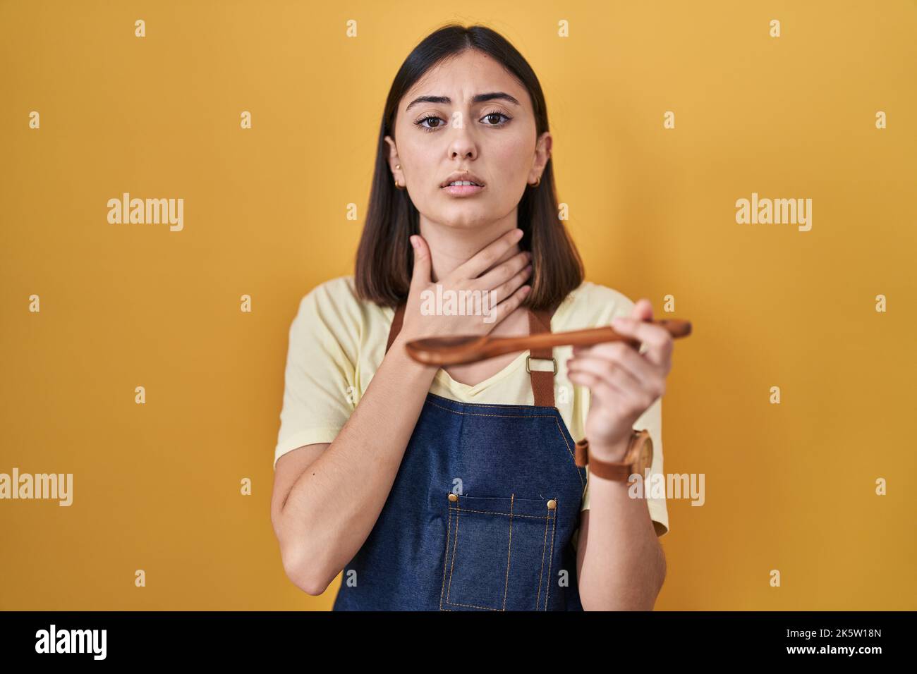Hispanic girl eating healthy wooden spoon touching painful neck, sore ...