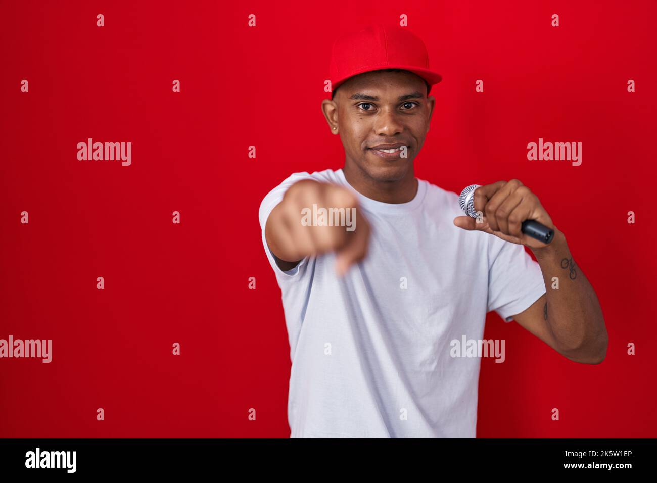 Young hispanic man singing song using microphone smiling happy pointing ...