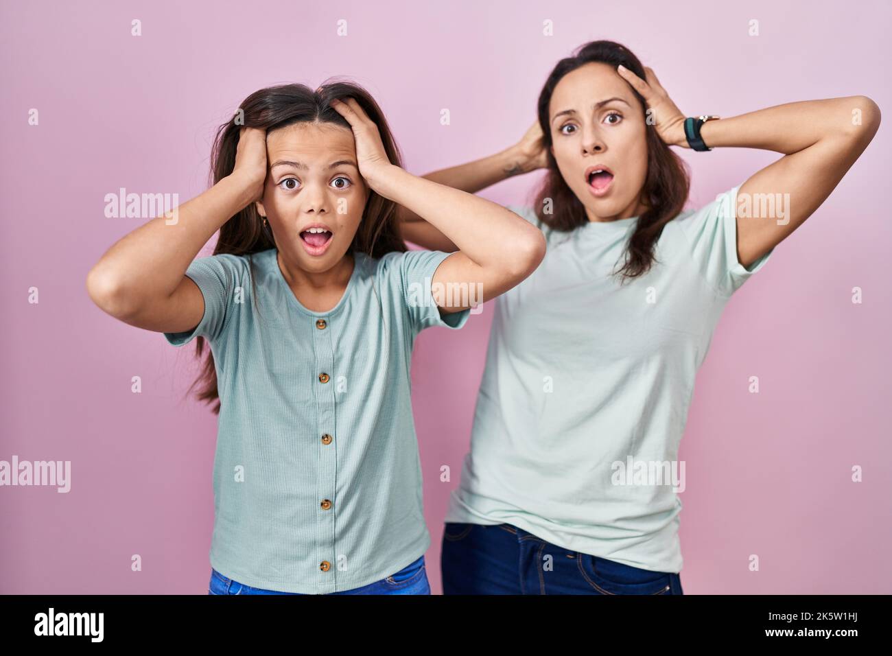 Young mother and daughter standing over pink background crazy and ...