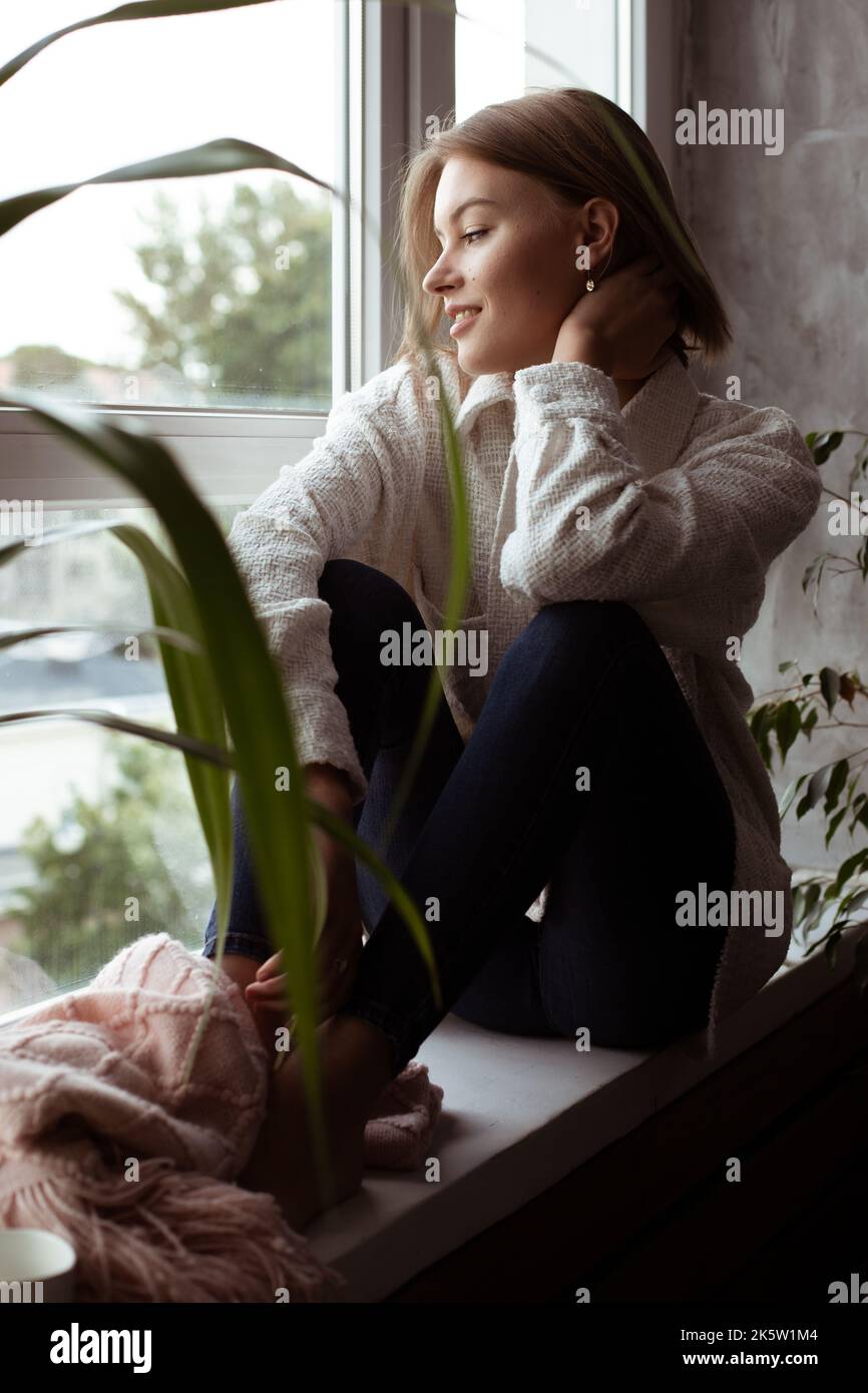 Vertical merry, calm, pensive romantic young woman looking out window ...