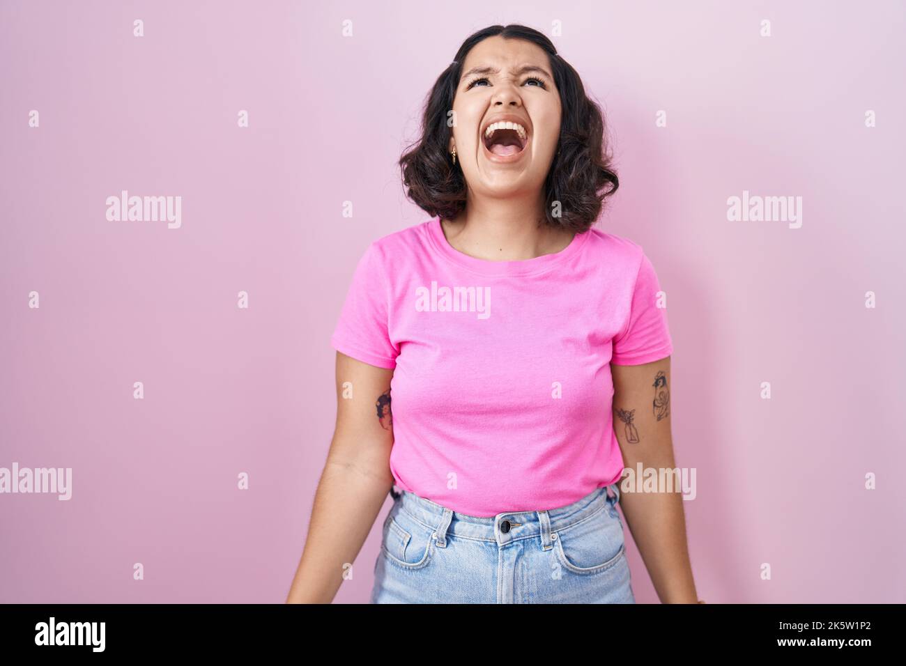 Young hispanic woman standing over pink background angry and mad ...