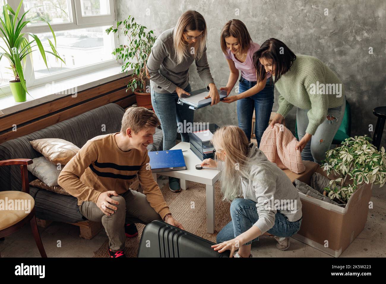 Smiling, energetic, busy friends packing luggage and trying to fit ...