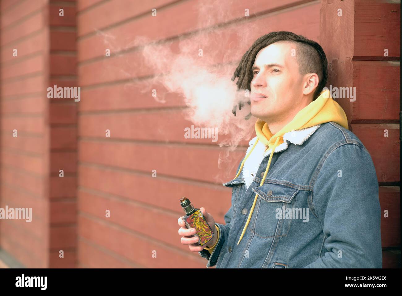Portrait of young handsome man with dreadlocks vaping, standing ...