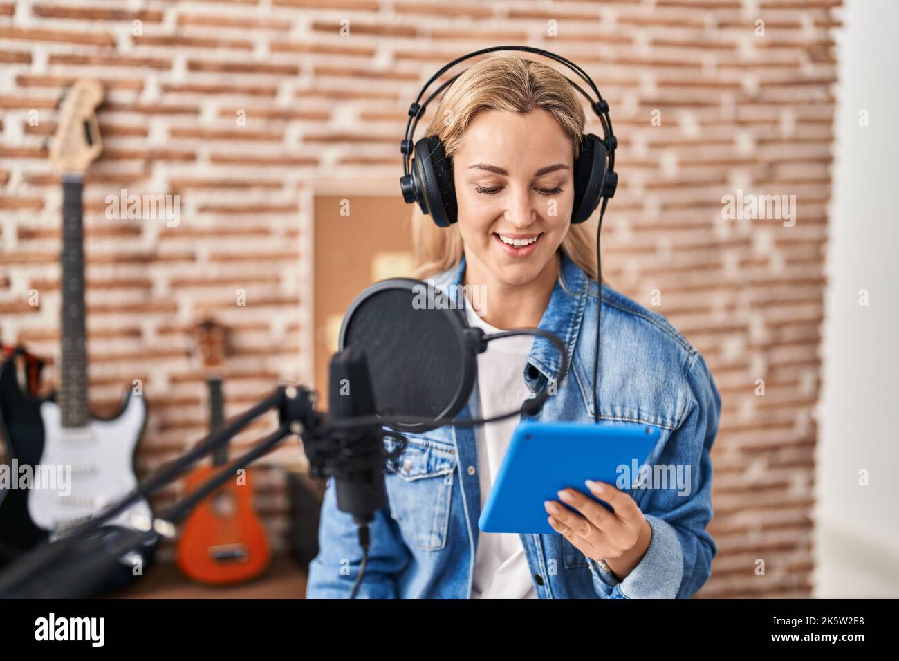 Young blonde woman artist singing song using touchpad at music studio ...