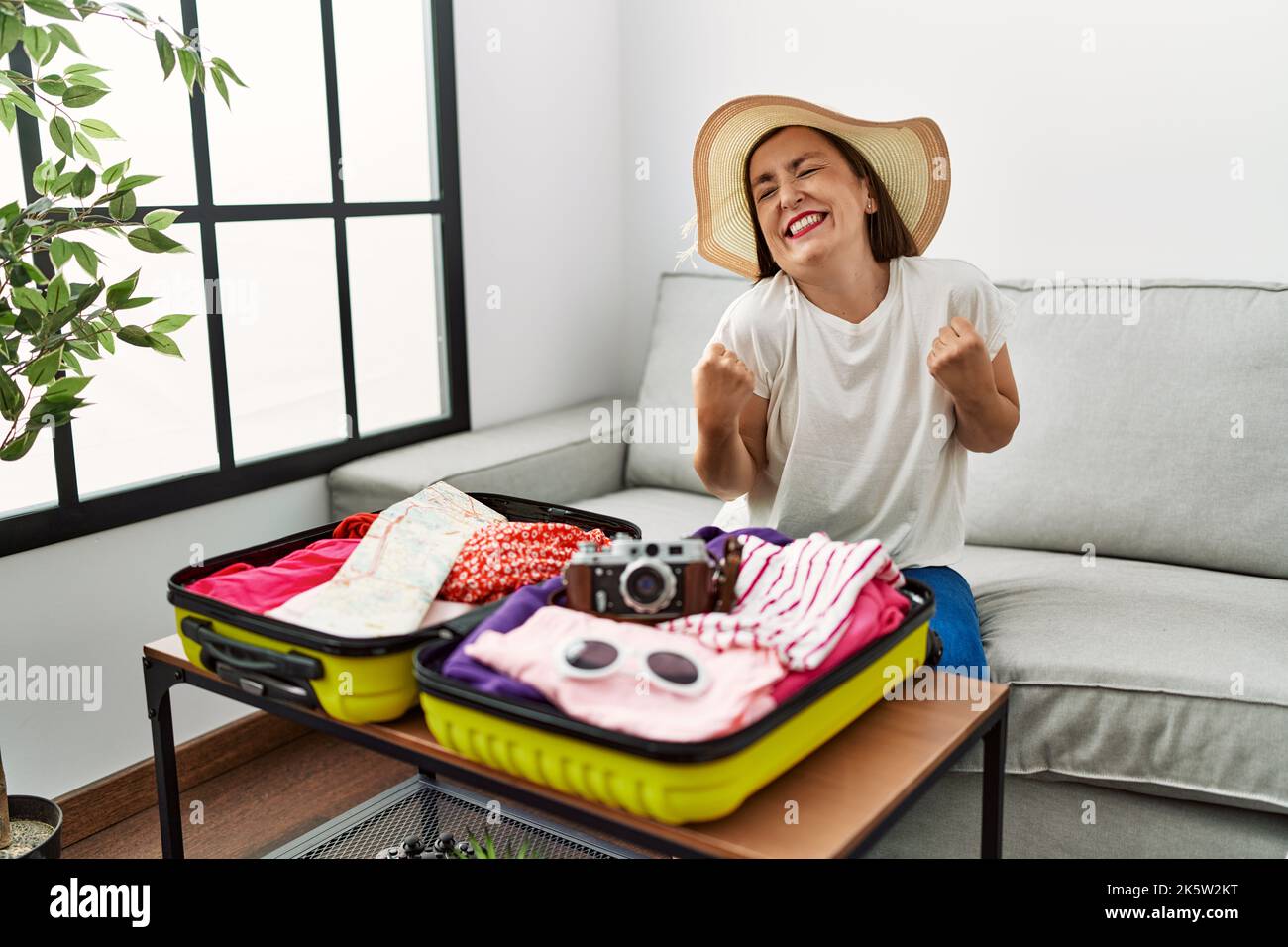Beautiful middle age hispanic woman packing summer clothes in suitcase ...