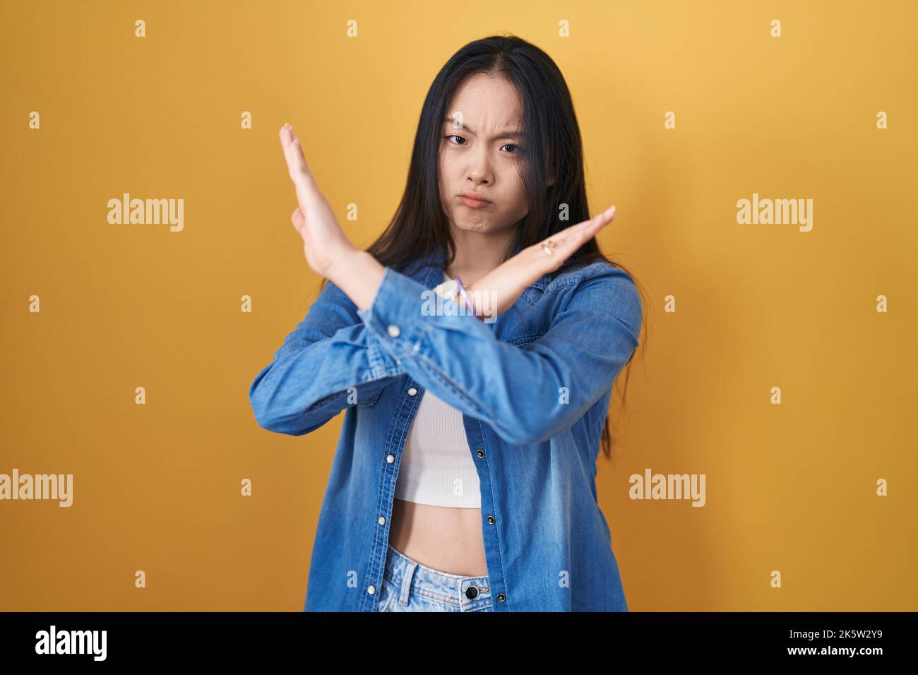 Young asian woman standing over yellow background rejection expression ...