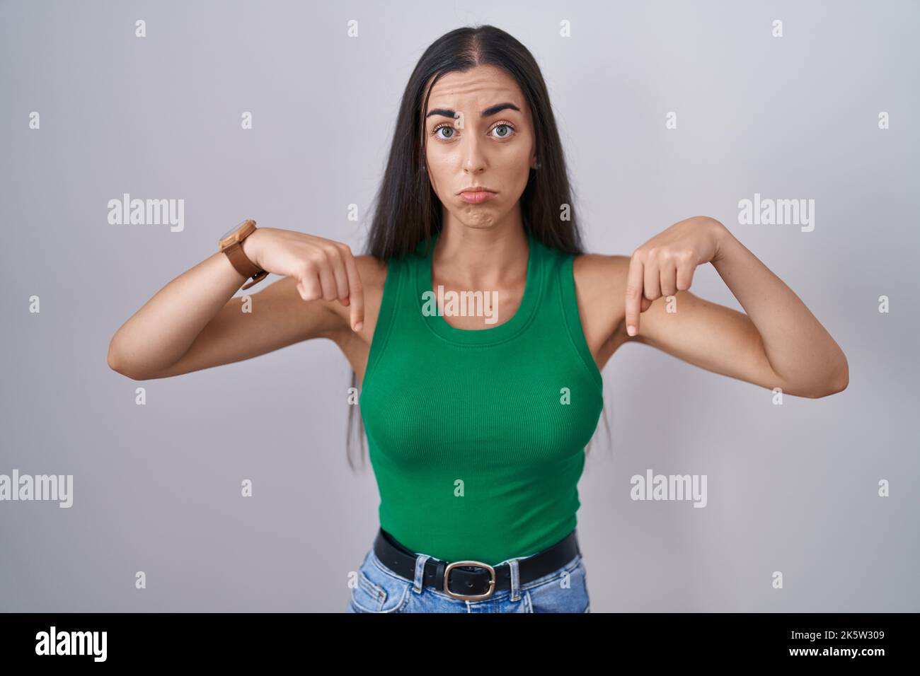 Young woman standing over isolated background pointing down looking sad ...