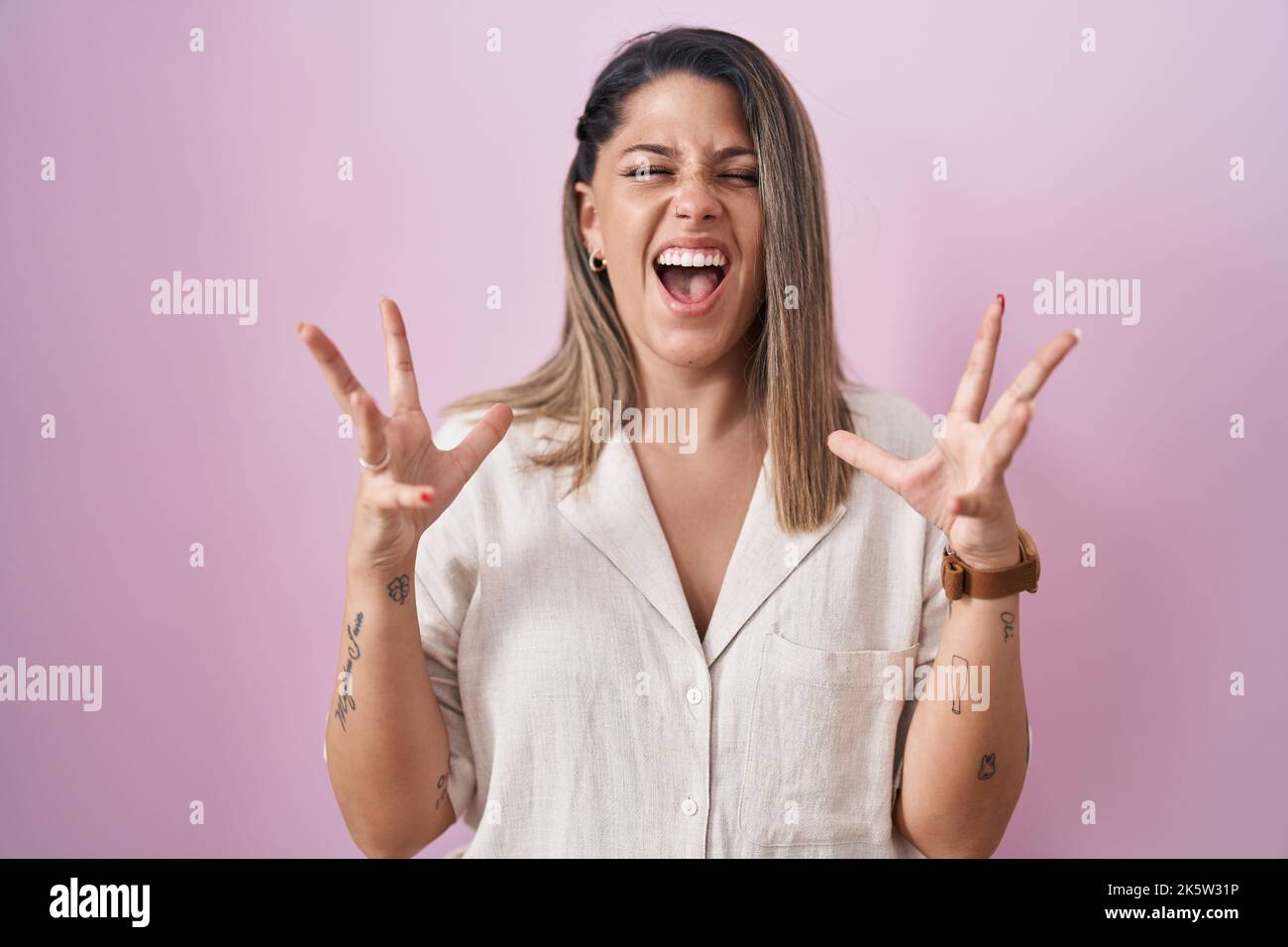 Blonde woman standing over pink background crazy and mad shouting and ...