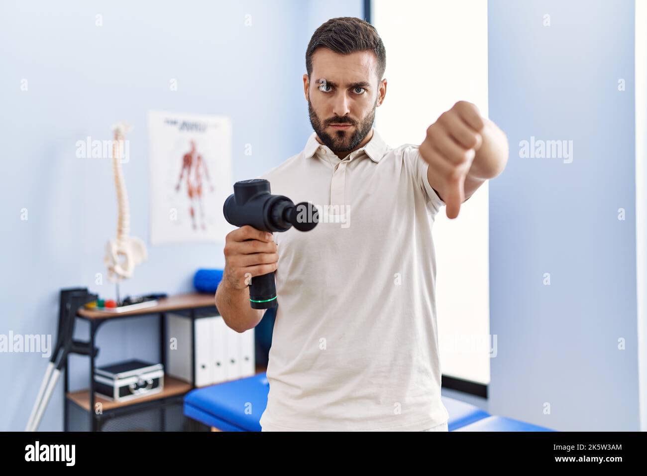 Handsome hispanic man holding therapy massage gun at physiotherapy ...