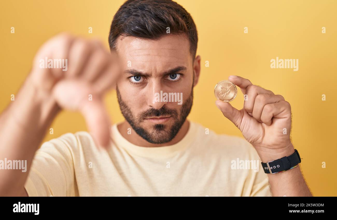 Handsome hispanic man holding uniswap cryptocurrency coin with angry ...