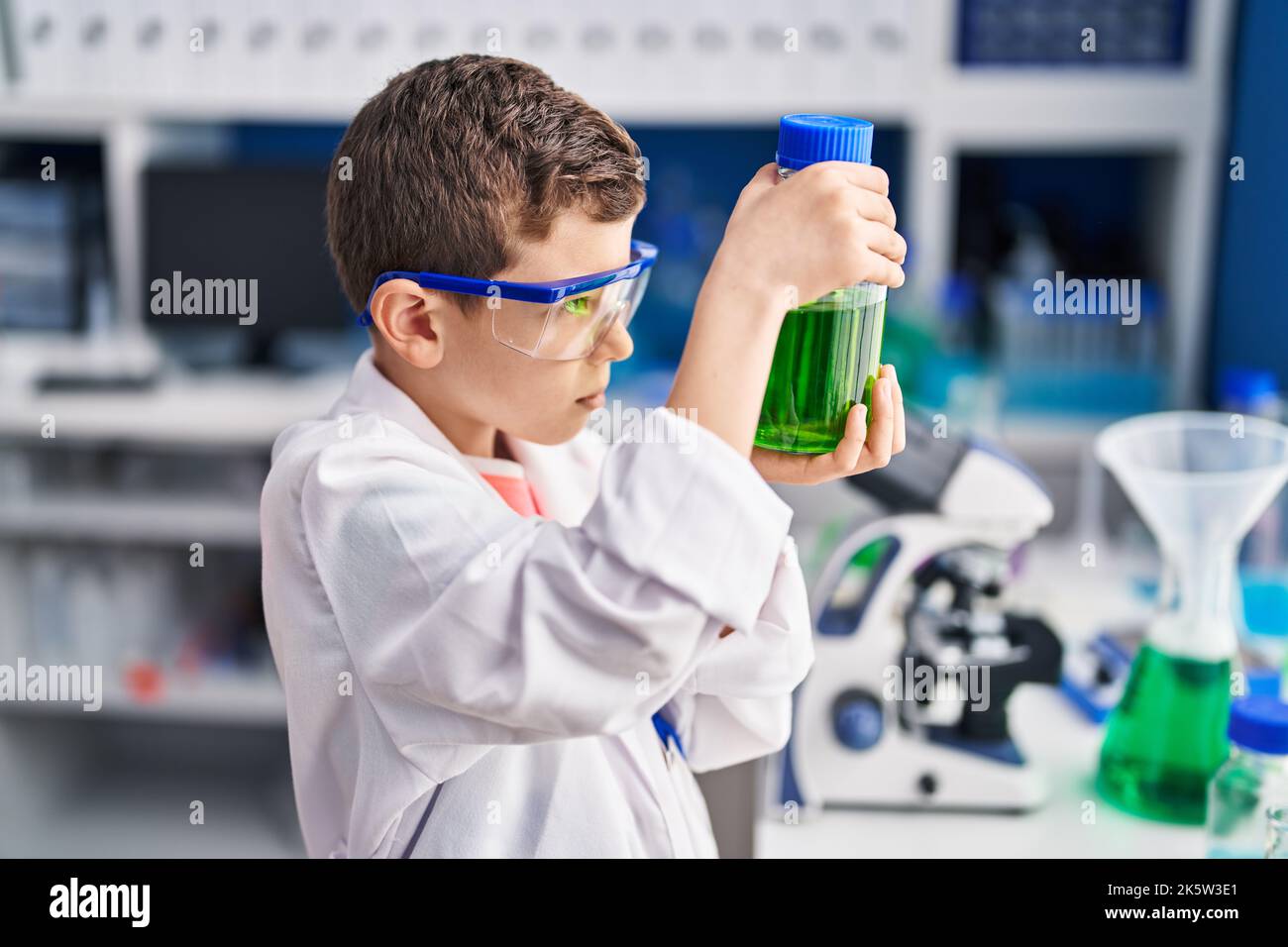 Blond child wearing scientist uniform holding bottle at laboratory ...