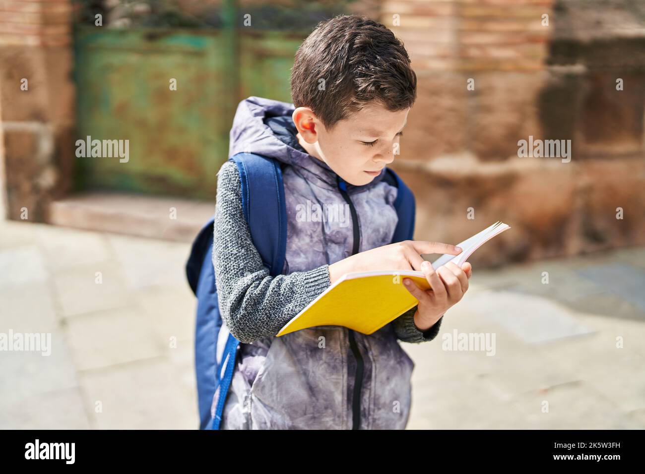 Blond child student reading book standing at street Stock Photo - Alamy
