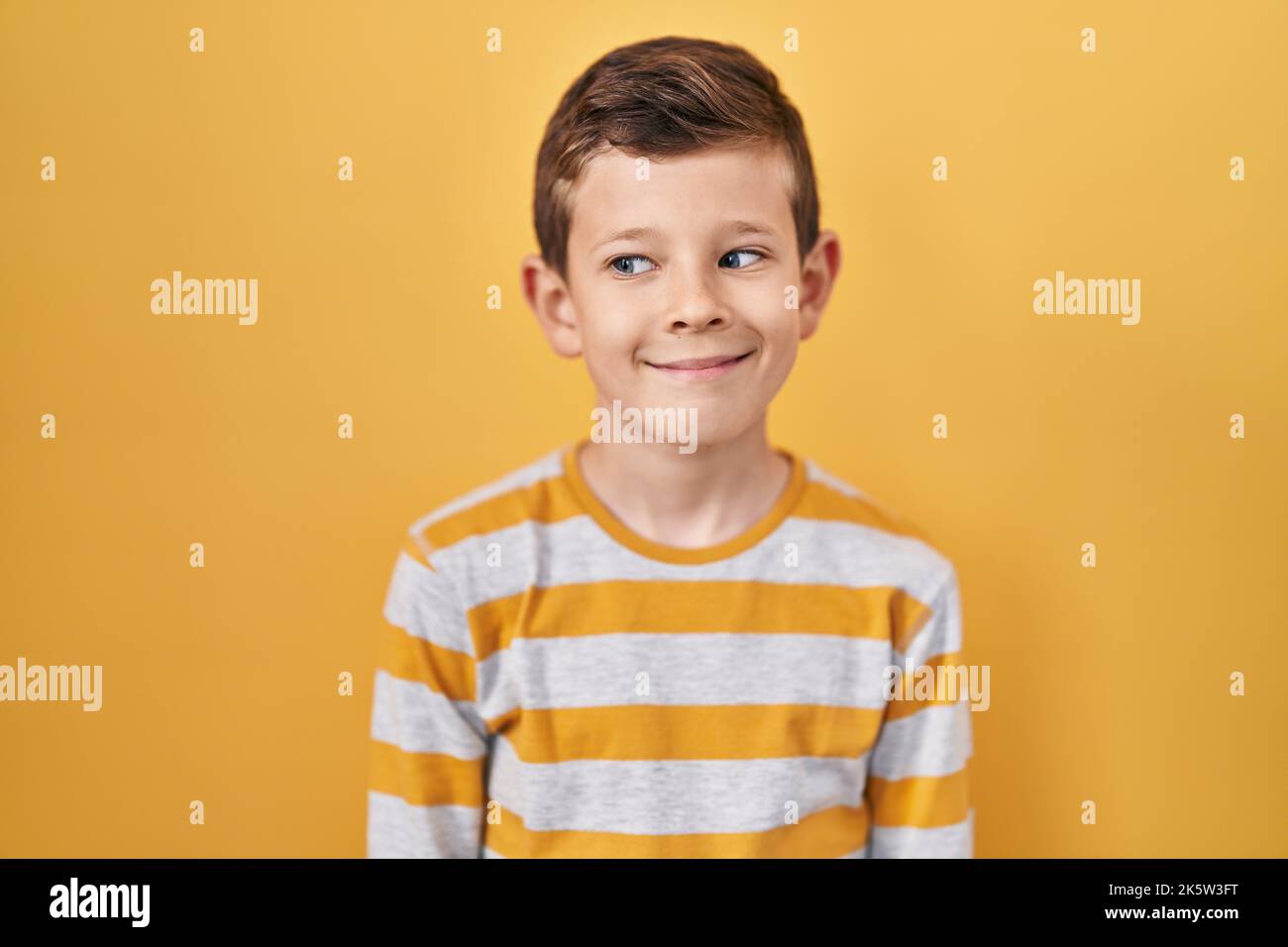 Young caucasian kid standing over yellow background smiling looking to ...