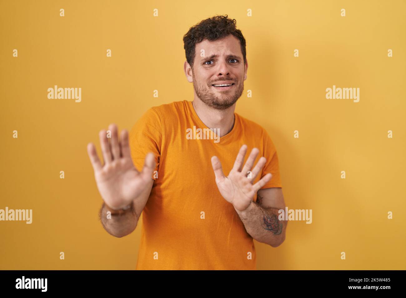 Young hispanic man standing over yellow background afraid and terrified ...