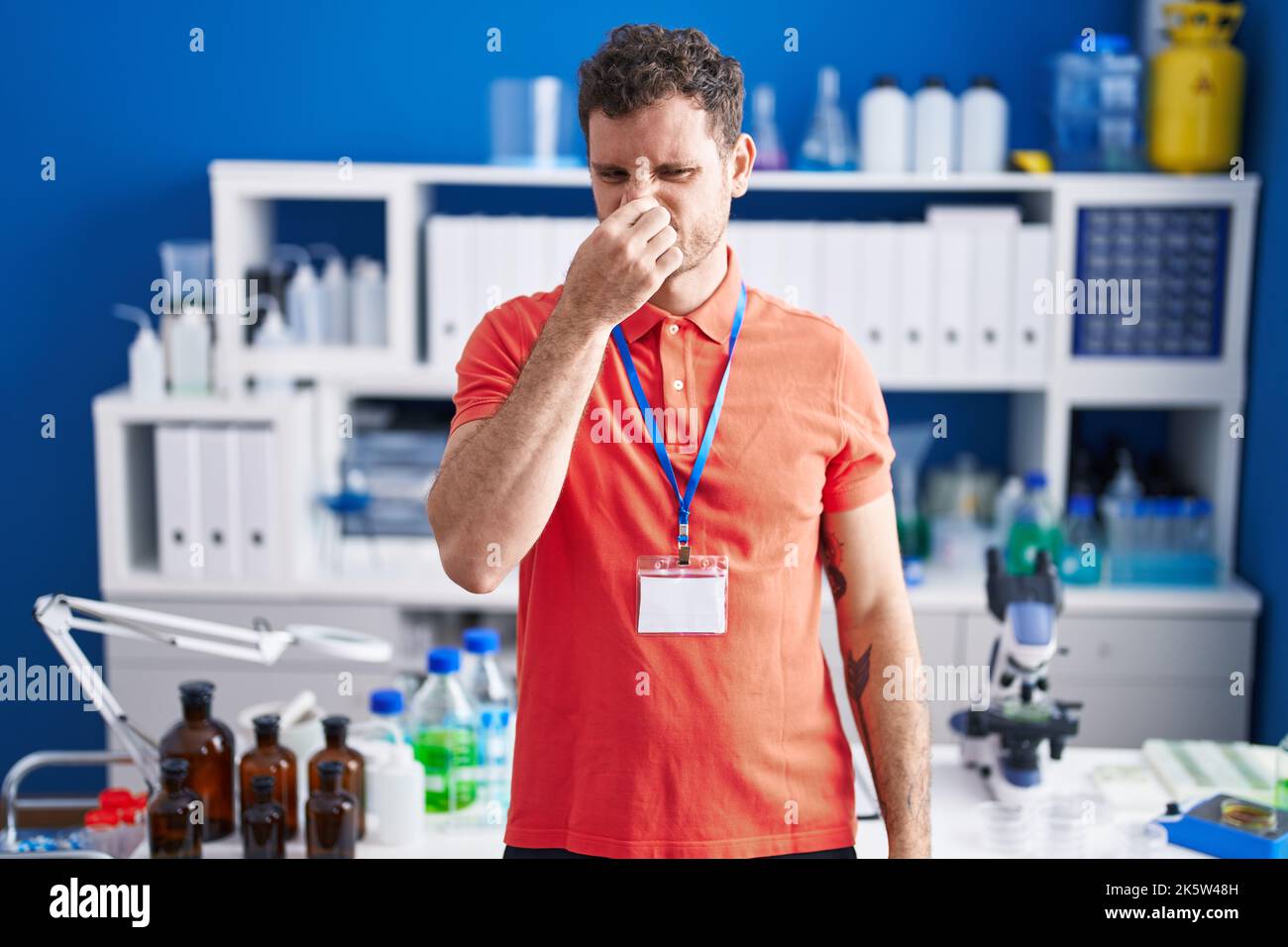 Young hispanic man working at scientist laboratory smelling something ...