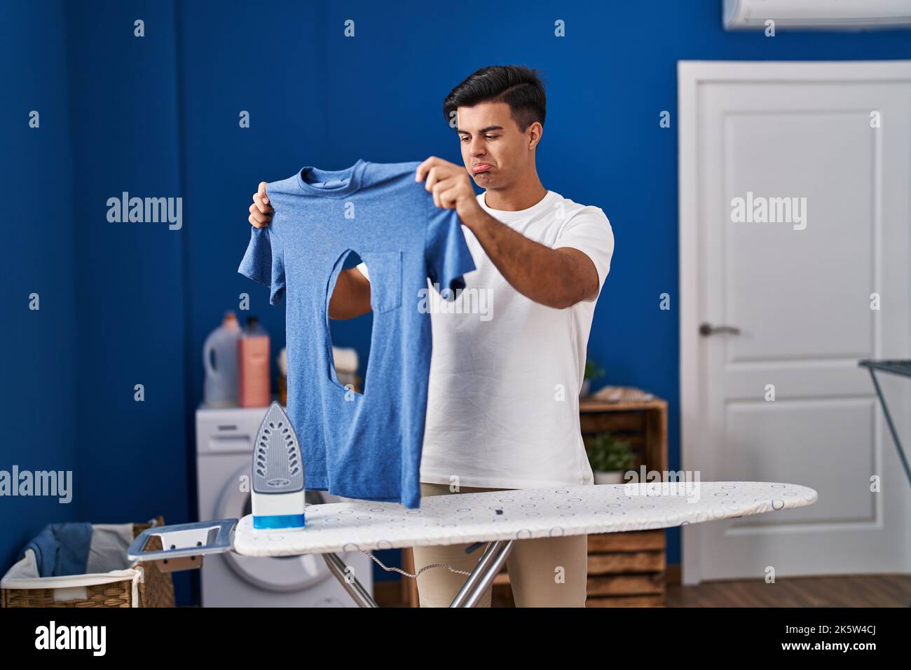 Hispanic man ironing holding burned iron shirt at laundry room ...